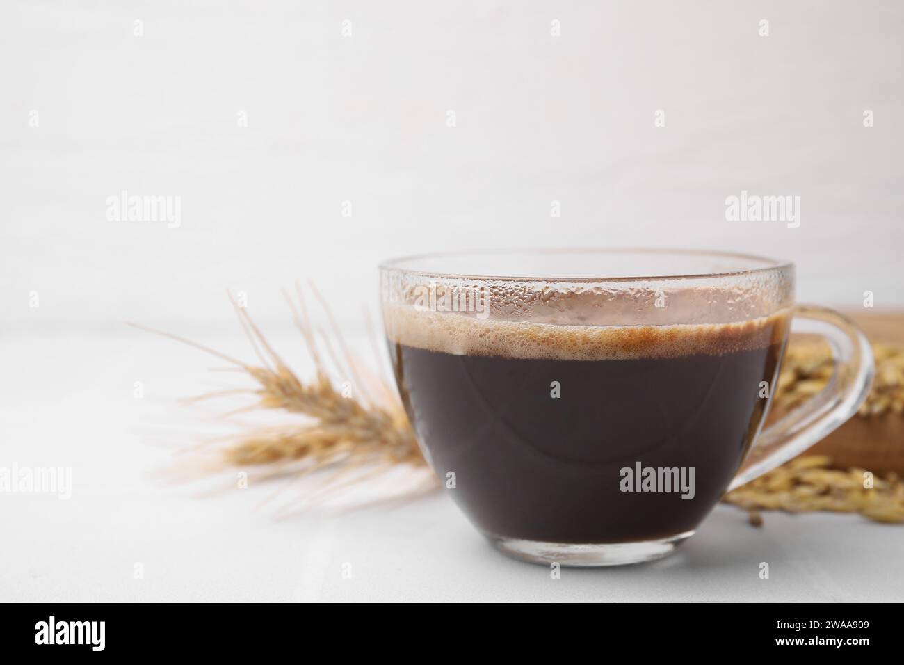 Cup of barley coffee and spike on white table, closeup. Space for text ...