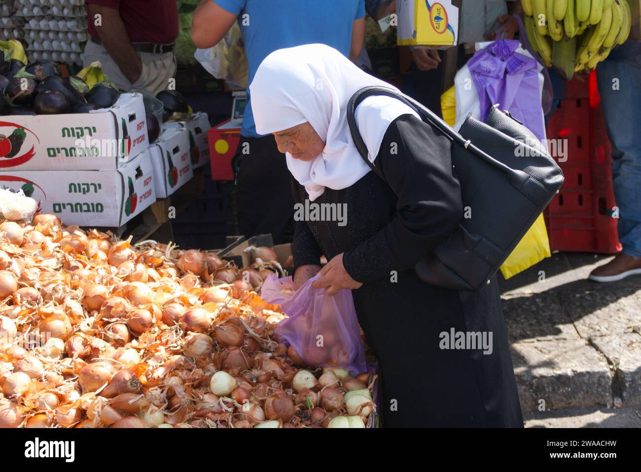 An elderly woman in traditional attire carefully selects onions at a ...