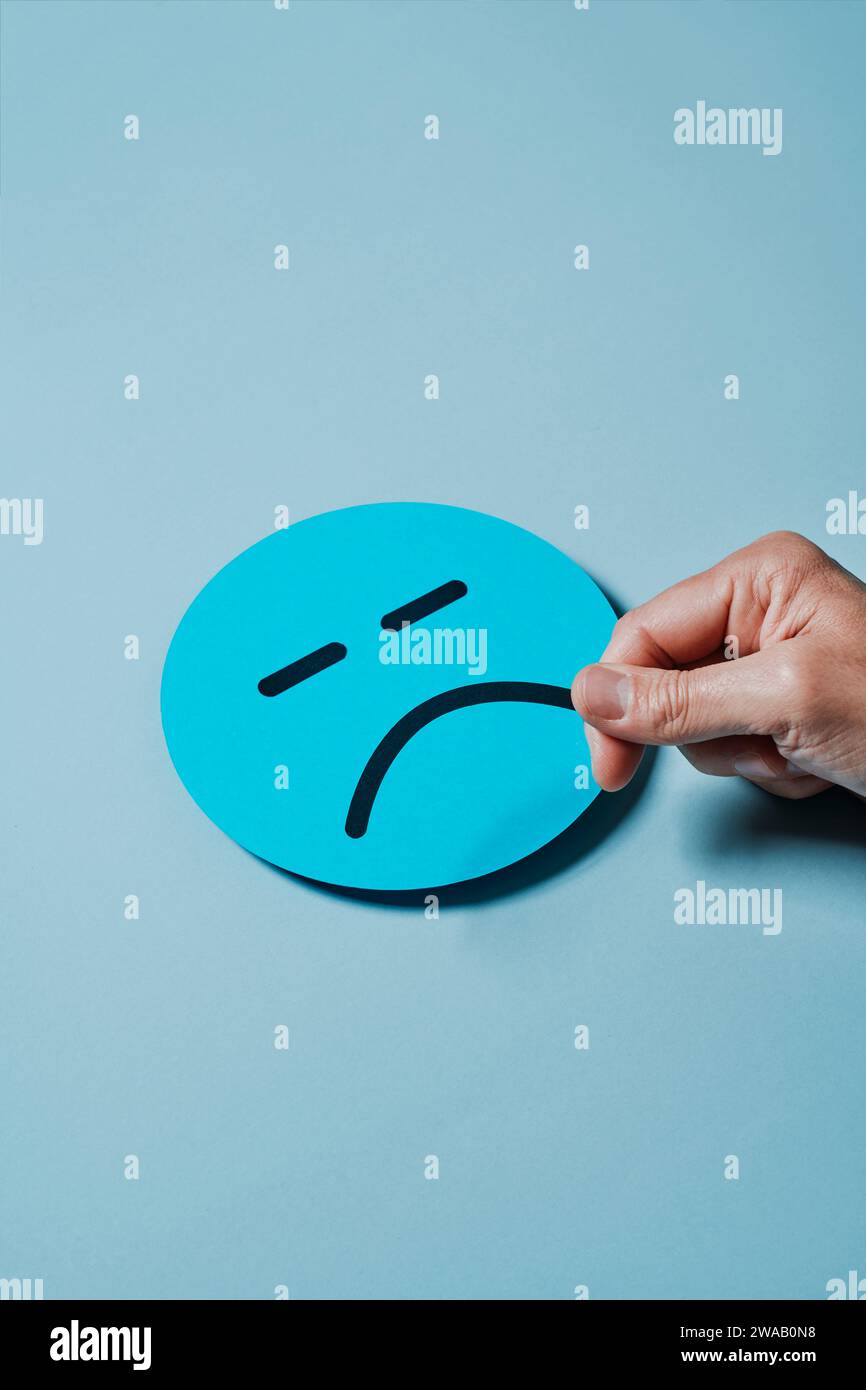 a man attaches a sad mouth to a blue cardboard face against a gray ...