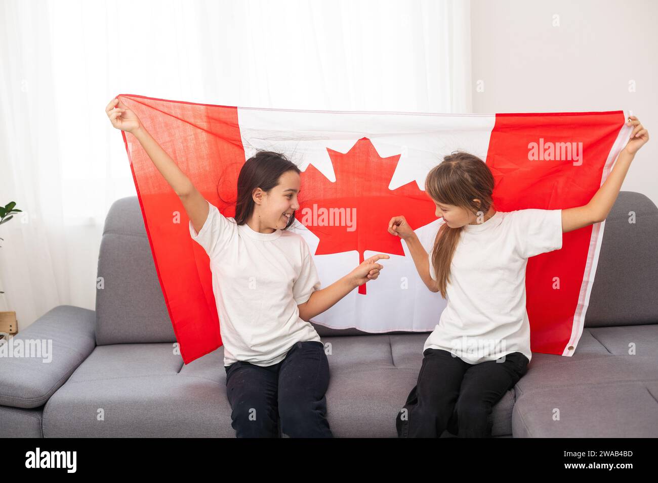 Two sisters are sitting on a couch at home with canadian flags on hands ...