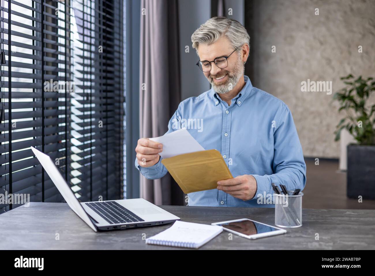 Smiling senior man sitting at home at work desk with laptop, opening ...