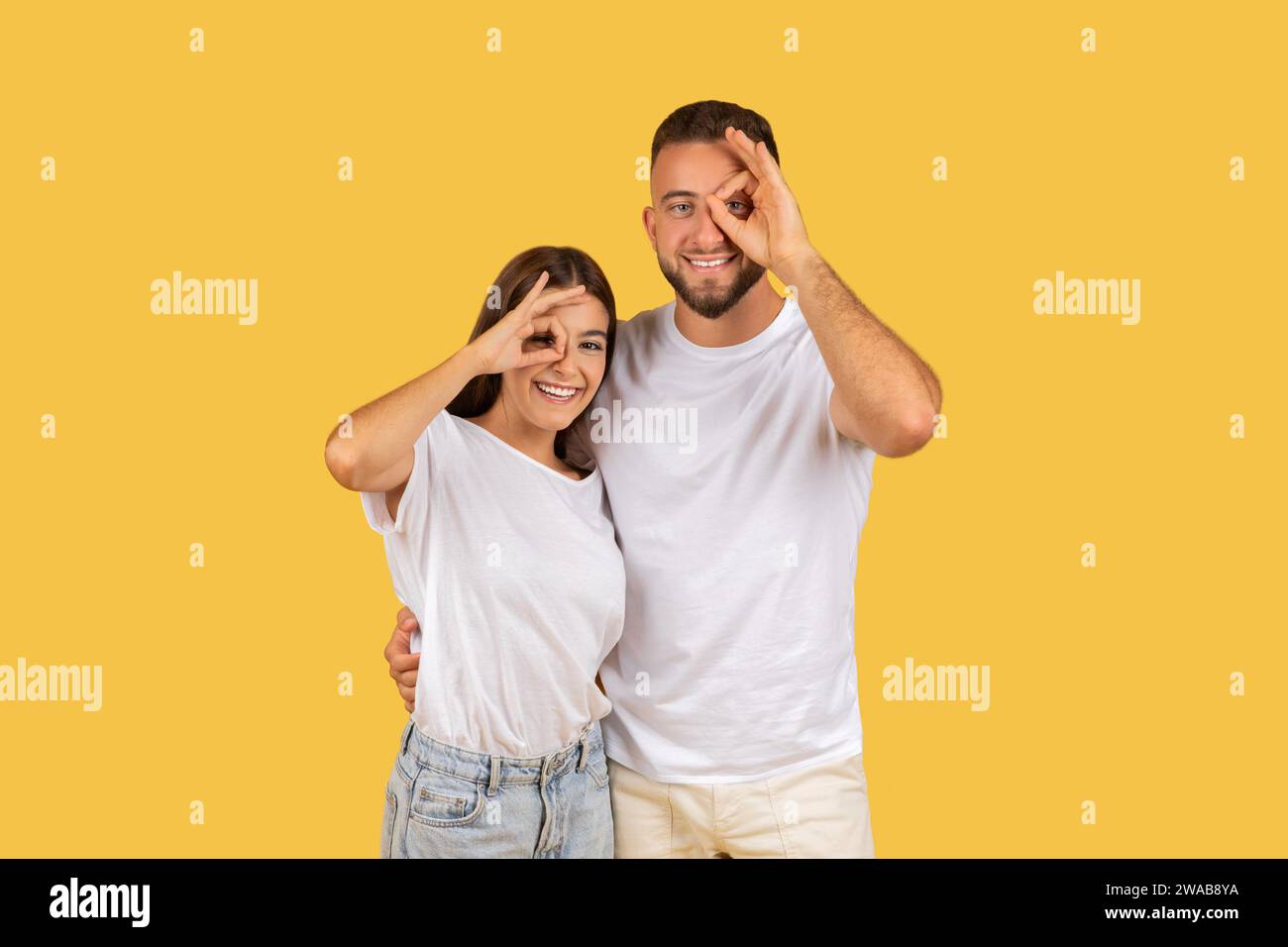 Playful young couple in white t-shirts making fun gestures with their ...