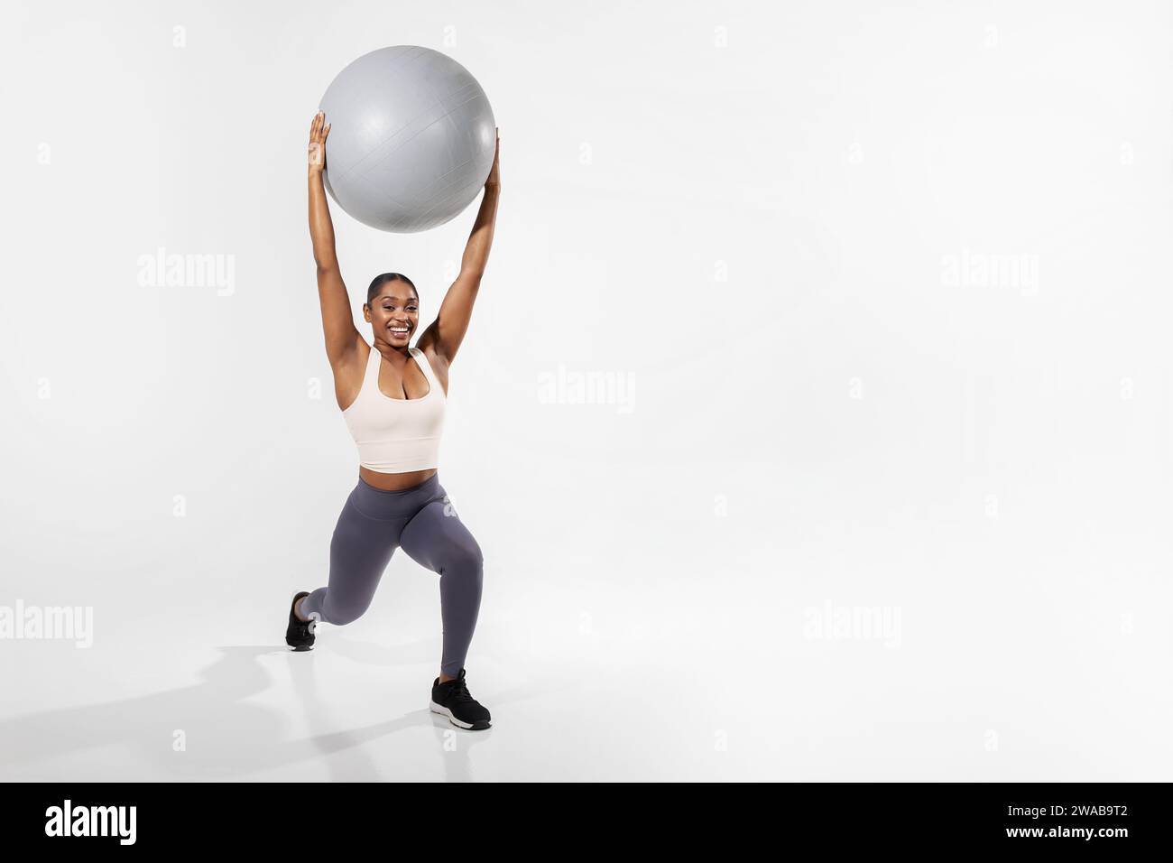 black woman in fitwear lifting stability ball while exercising, studio ...