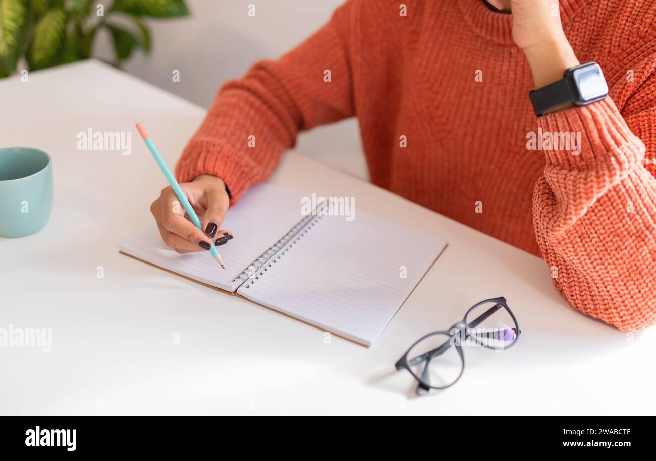 Professional woman in sweater writing notes on pad, wearing smartwatch ...