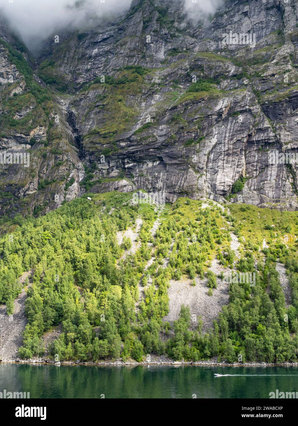 A tiny boat passing under a typical massive cliffs on the side of the ...