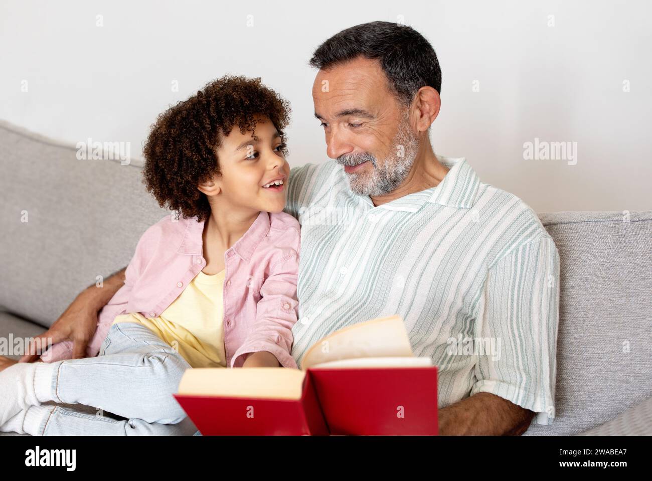 Senior Latin grandfather reading book to his grandchild boy indoor ...