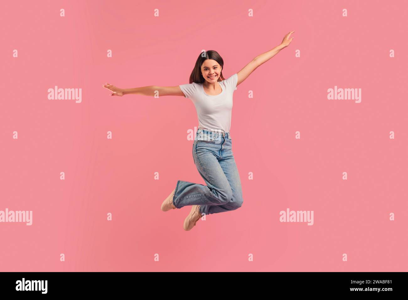 Joyful teenage girl mid-jumping with outstretched arms, expressing ...
