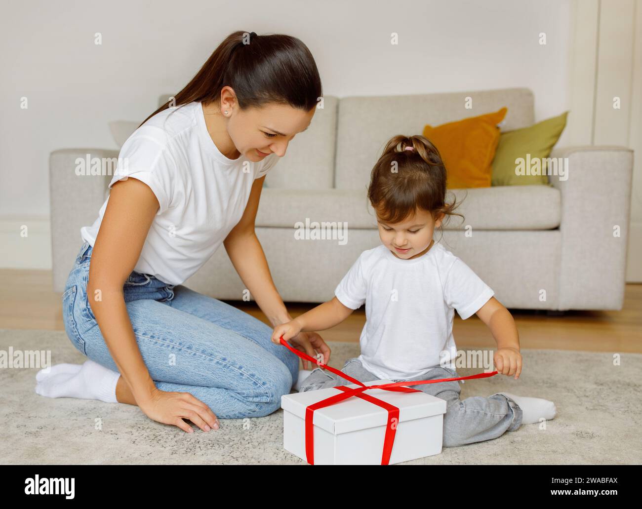 Adorable Little Girl Unpacking Gift Box With Red Ribbon At Home Stock ...