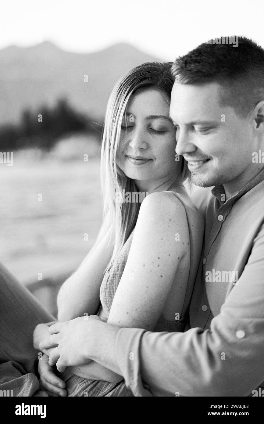 Man Hugs Woman From Behind While Sitting With Her On The Seashore