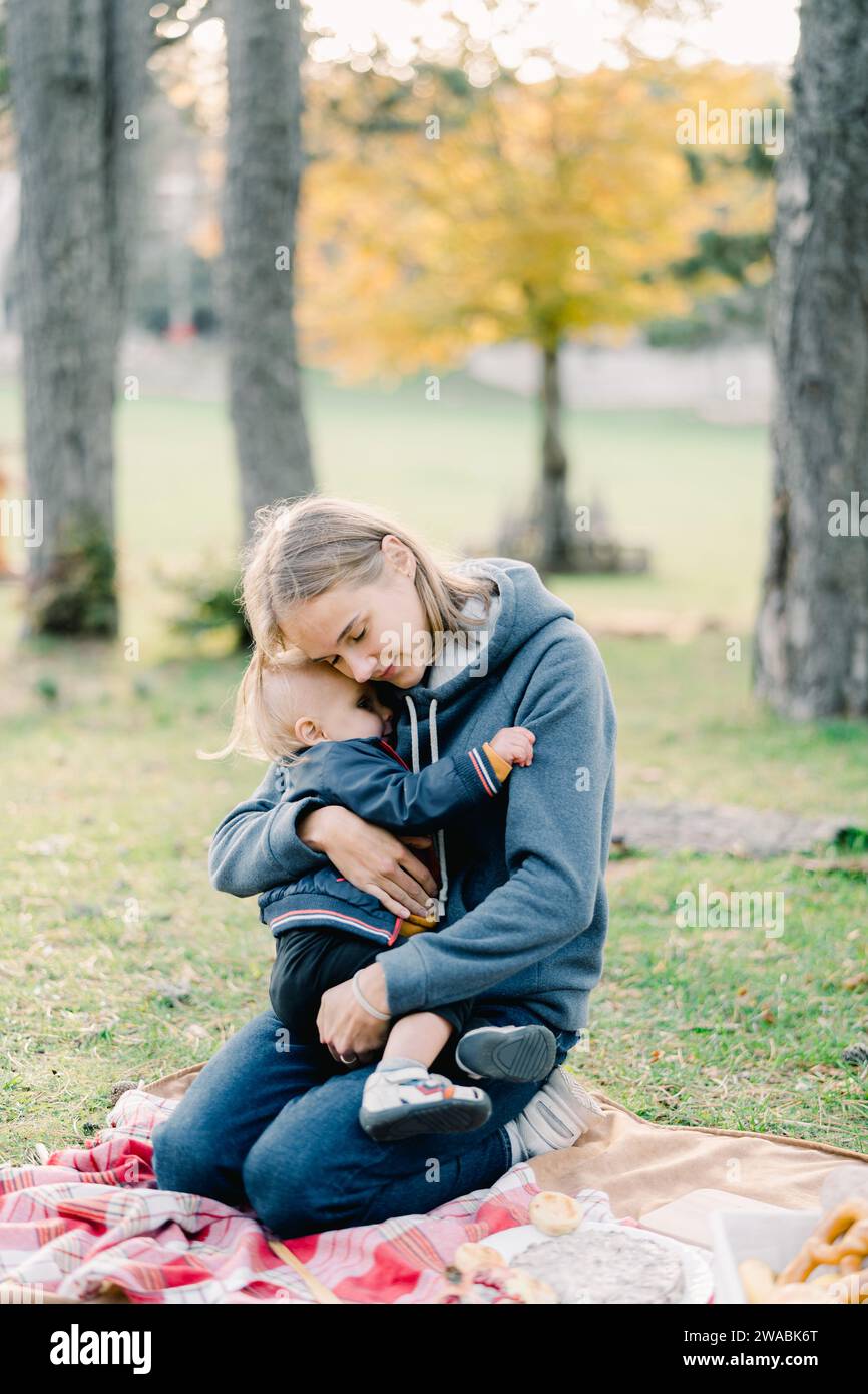 Mom hugs a little boy sitting on her lap on a blanket in the park Stock Photo - Alamy