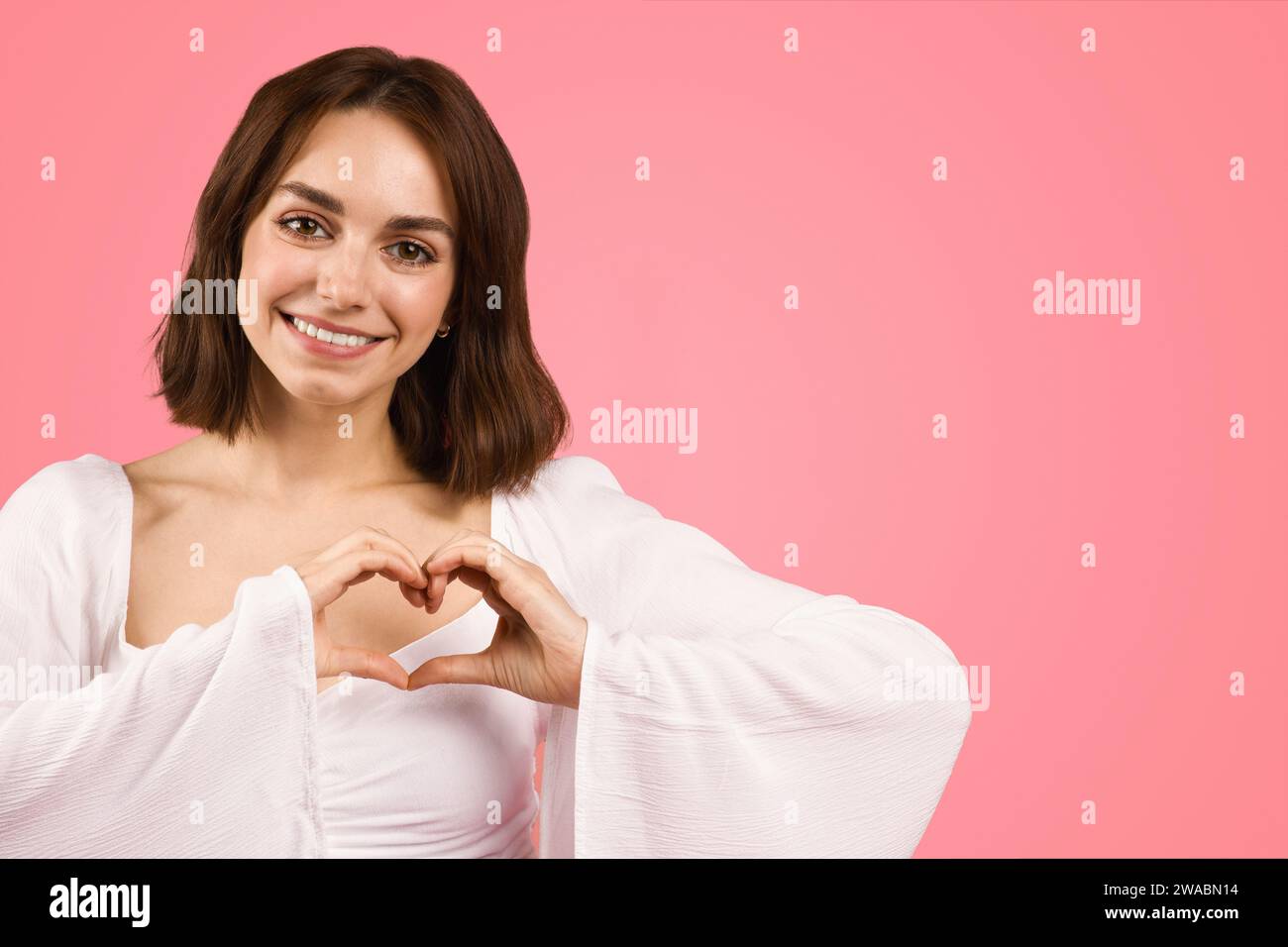 A cheerful young woman with a heartwarming smile makes a heart shape ...