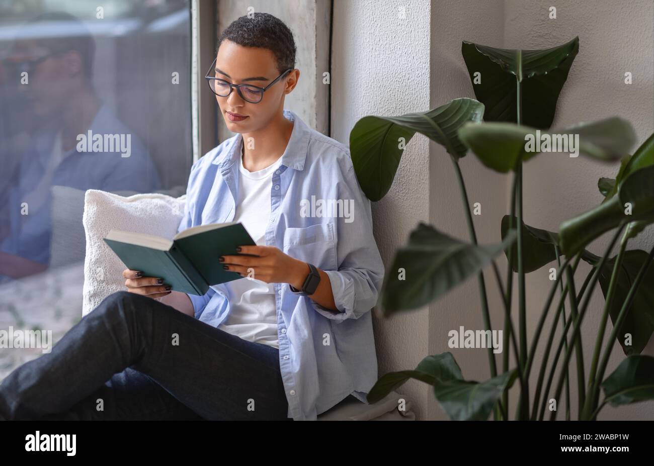 Reflective and relaxed young woman reading a book by the window Stock ...