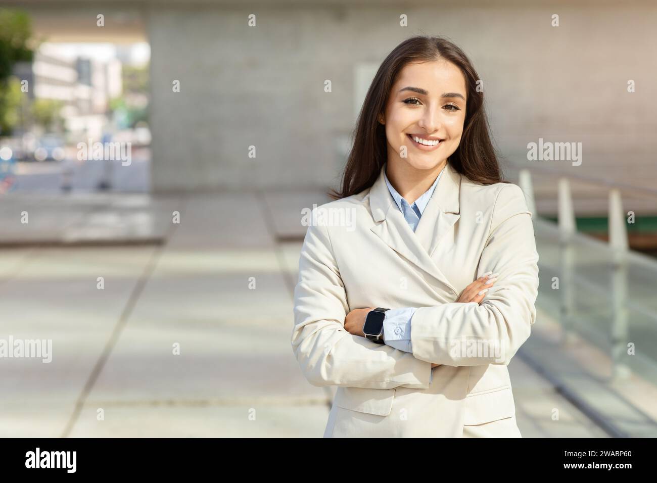 Smiling young professional woman confidently standing with arms crossed ...