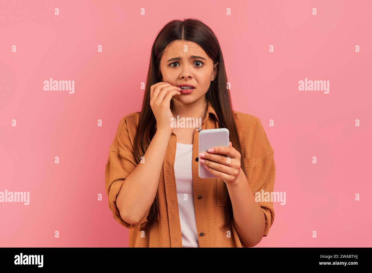 Anxious teenage girl biting her nails while looking at smartphone Stock ...