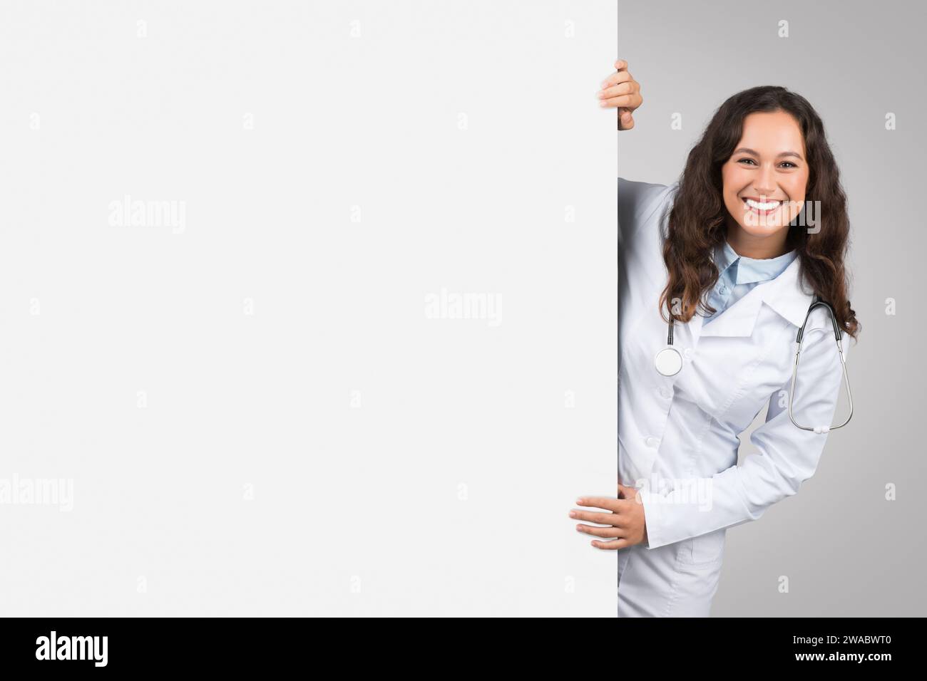 Medical ad. Happy european woman doctor peeking out of huge blank ...