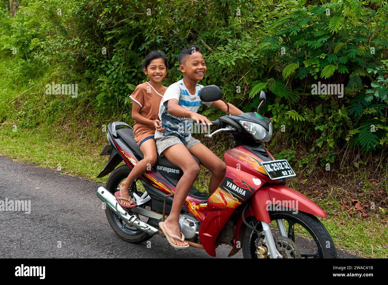 Children ride a scooter without helmets on a road in a village in Asia ...