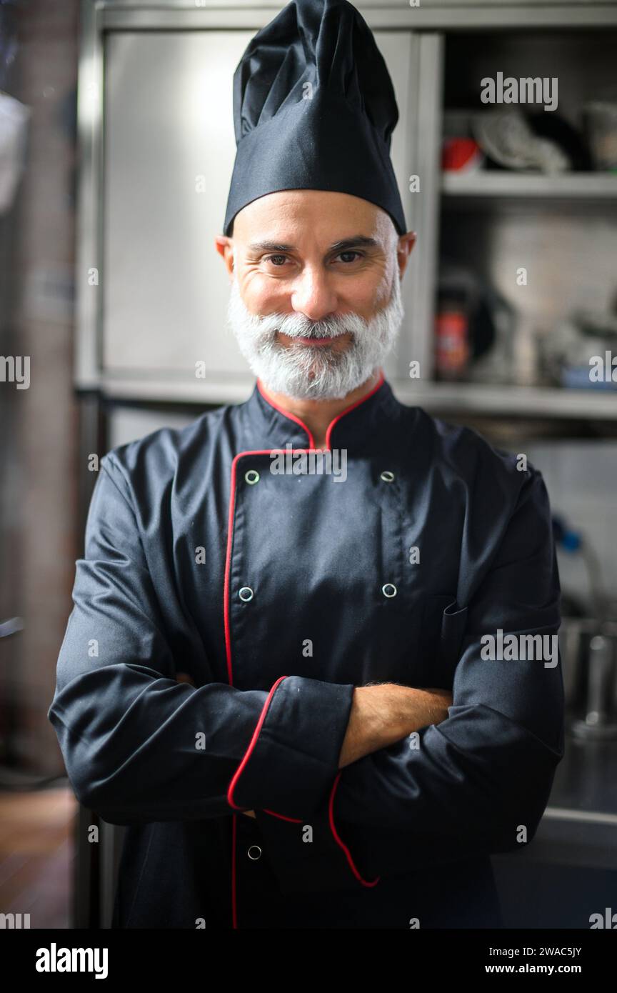 Mature chef in black coat with folded arms in his kitchen Stock Photo ...