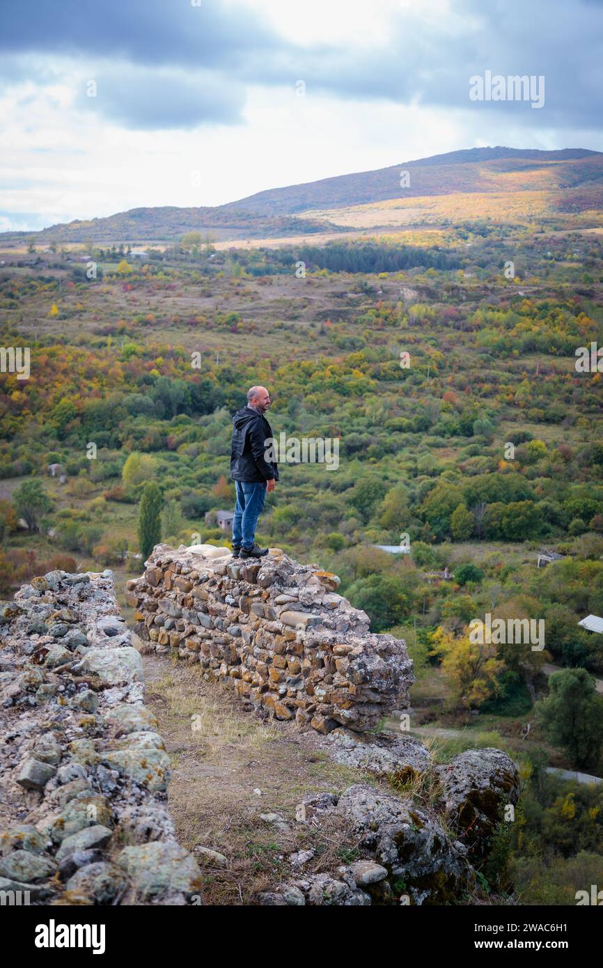 A lone figure stands at the edge of ancient mountain fortress ruins ...