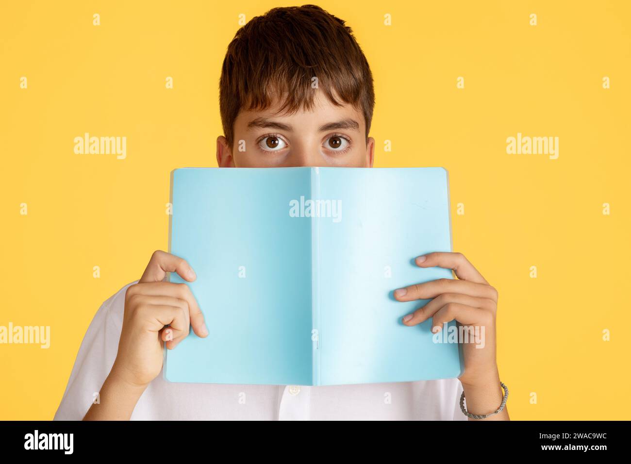 A boy with an intrigued expression carefully covers his face with a ...