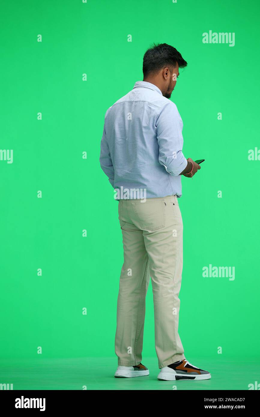 A man in a blue shirt, on a green background, full-length, with a phone ...