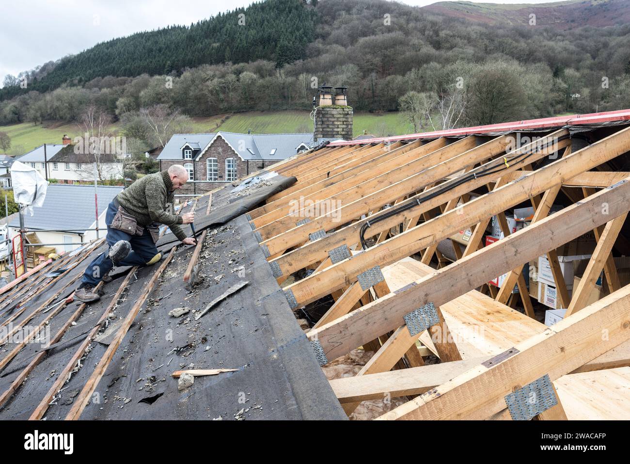 Roofer removing old batons and felt from pitched roof on house ...