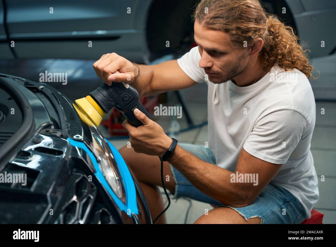Long-haired guy with muscular arms cleans the headlights of car Stock ...
