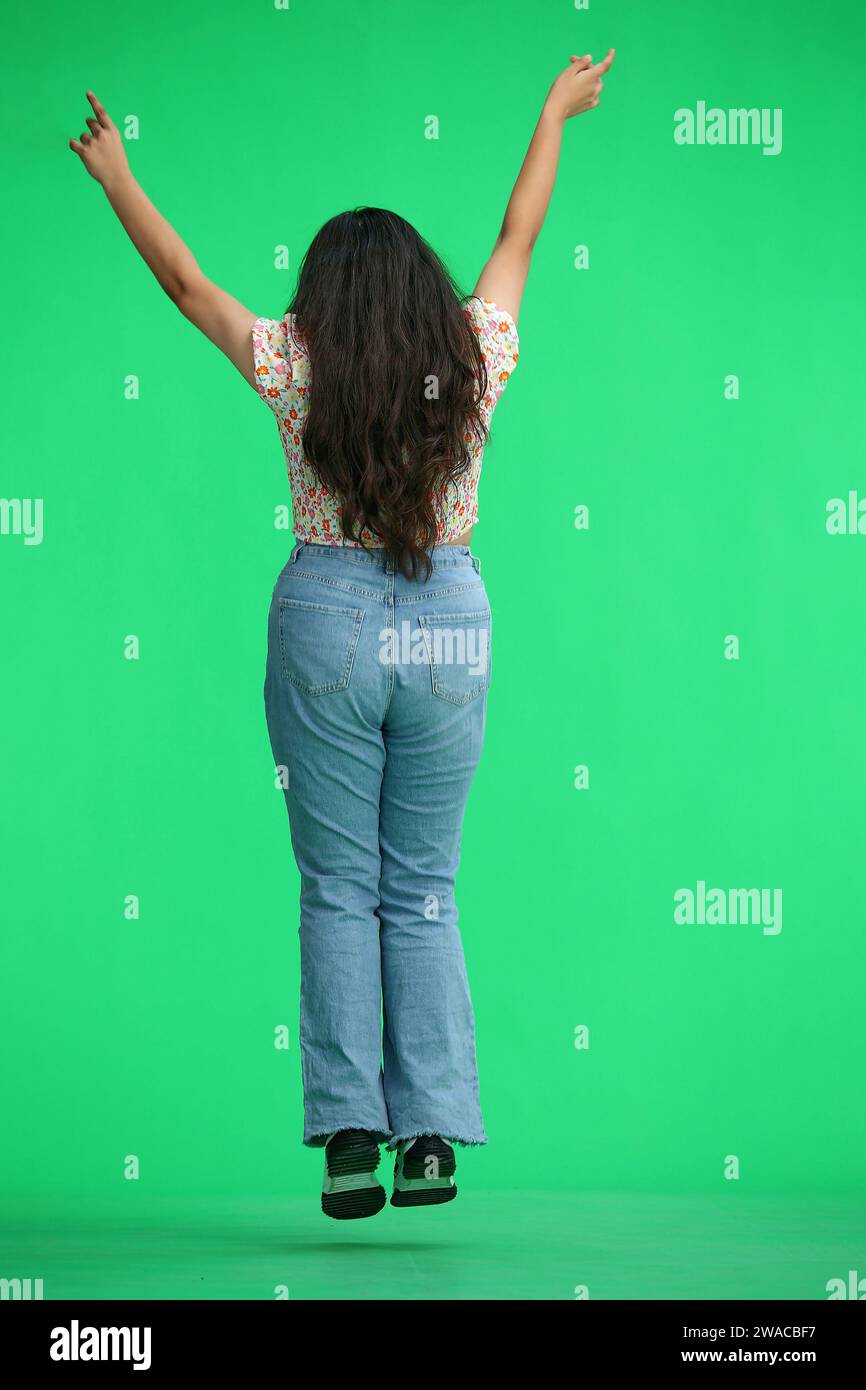 A woman, on a green background, in full height, jumps with her hand ...