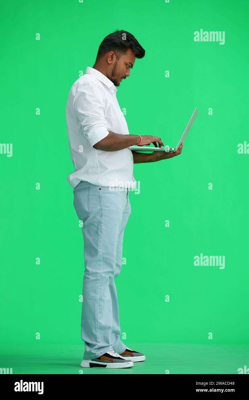 A man in a white shirt, on a green background, in full height, uses a ...