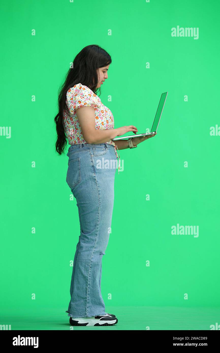 A woman, on a green background, in full height, uses a laptop, profile ...