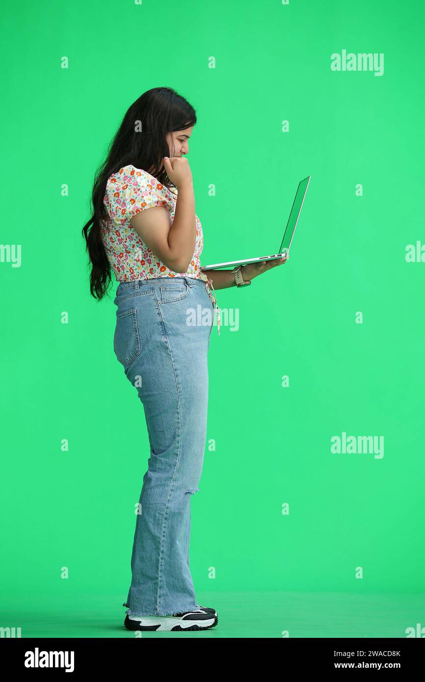A woman, on a green background, in full height, uses a laptop, profile ...