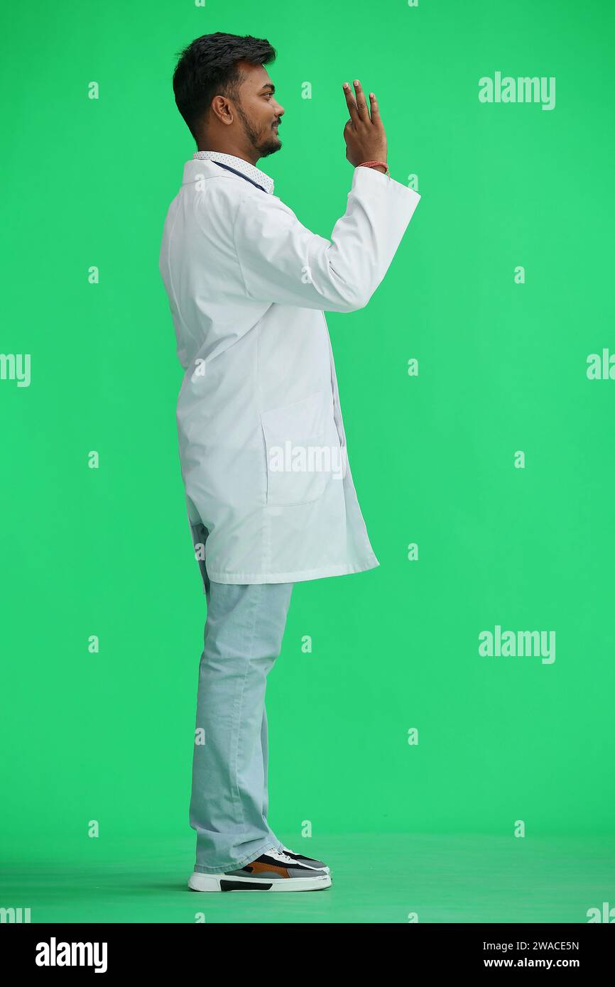 A male doctor, on a green background, in full height, shows the ok sign ...