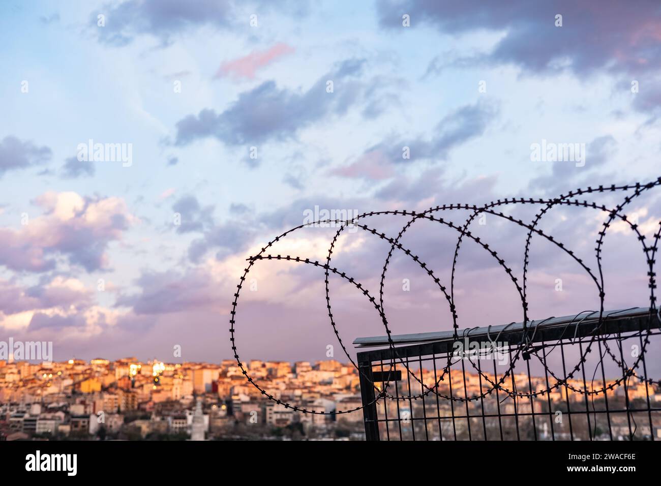 Sunset sky and barbed wire over a city. Barbed wire fence- restricted ...
