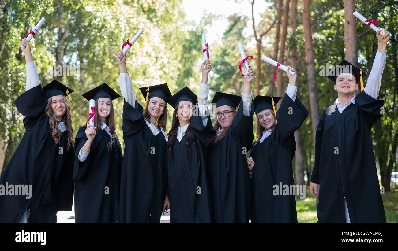 Row of young students in graduation gowns outdoors showing off their ...