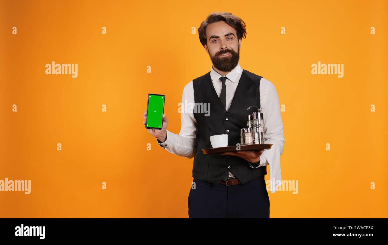 Bearded waiter presents greenscreen on phone display, holding ...