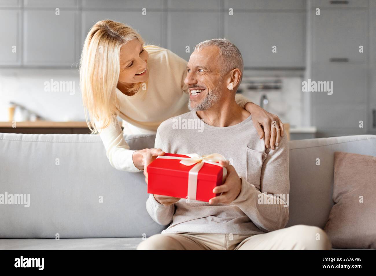 Loving mature woman giving present her surprised husband Stock Photo ...