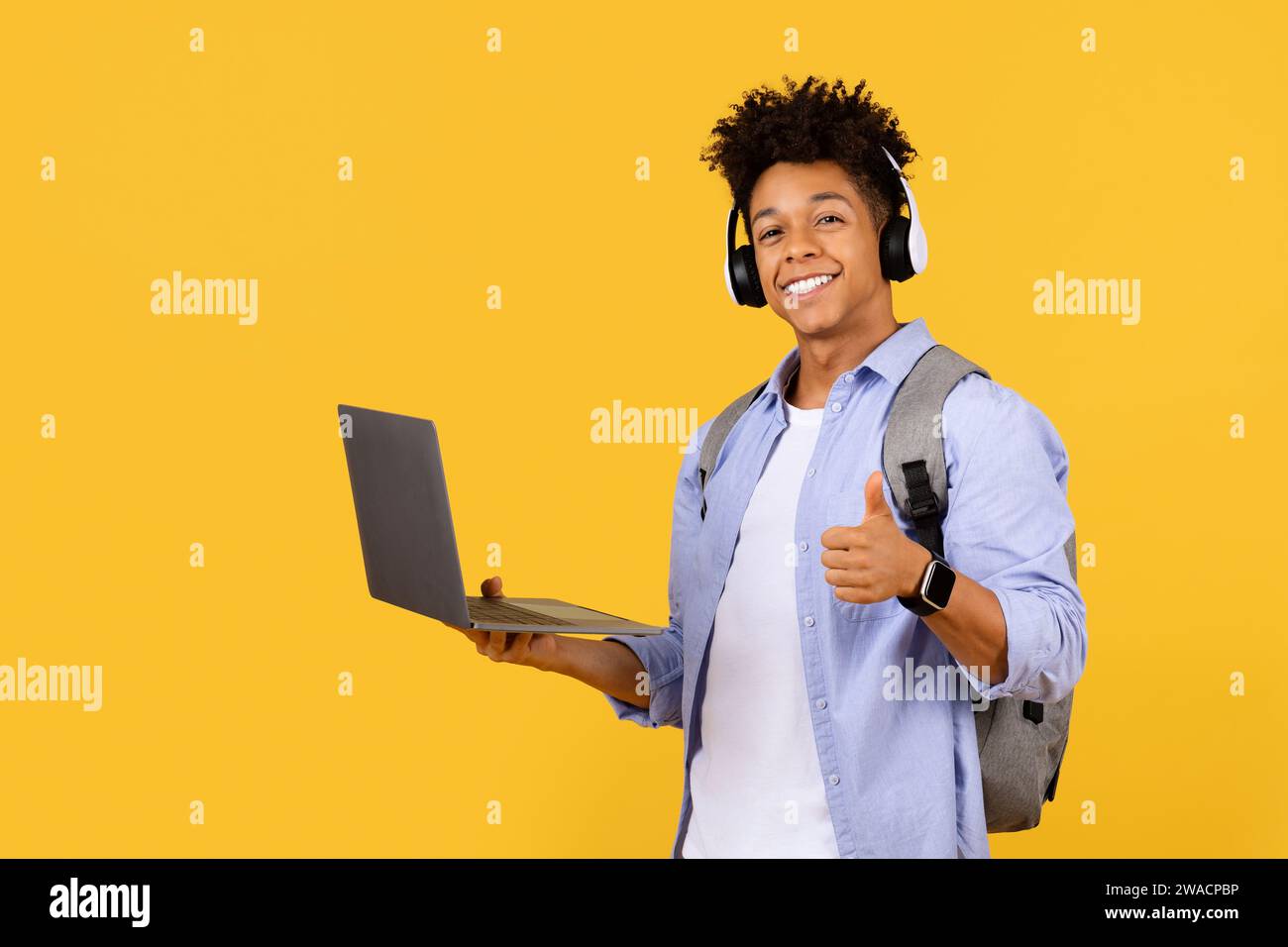 Upbeat black male student with laptop giving thumbs up on yellow Stock ...