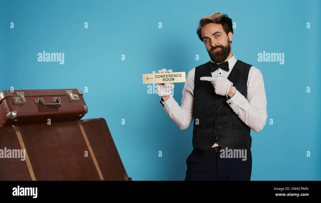 Elegant bellboy shows conference room symbol in hand, presenting wall ...