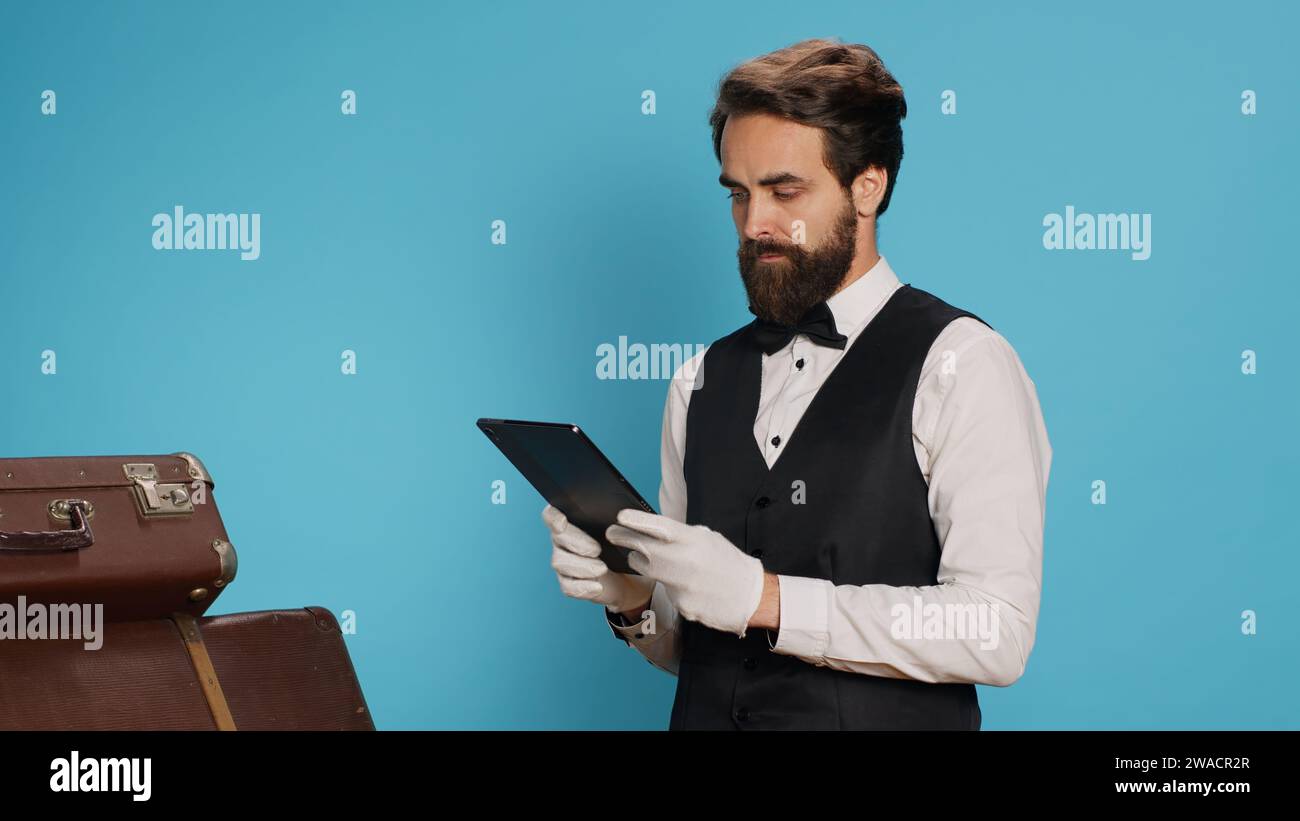 Male bellhop working on tablet, being in charge of trolley bags for ...