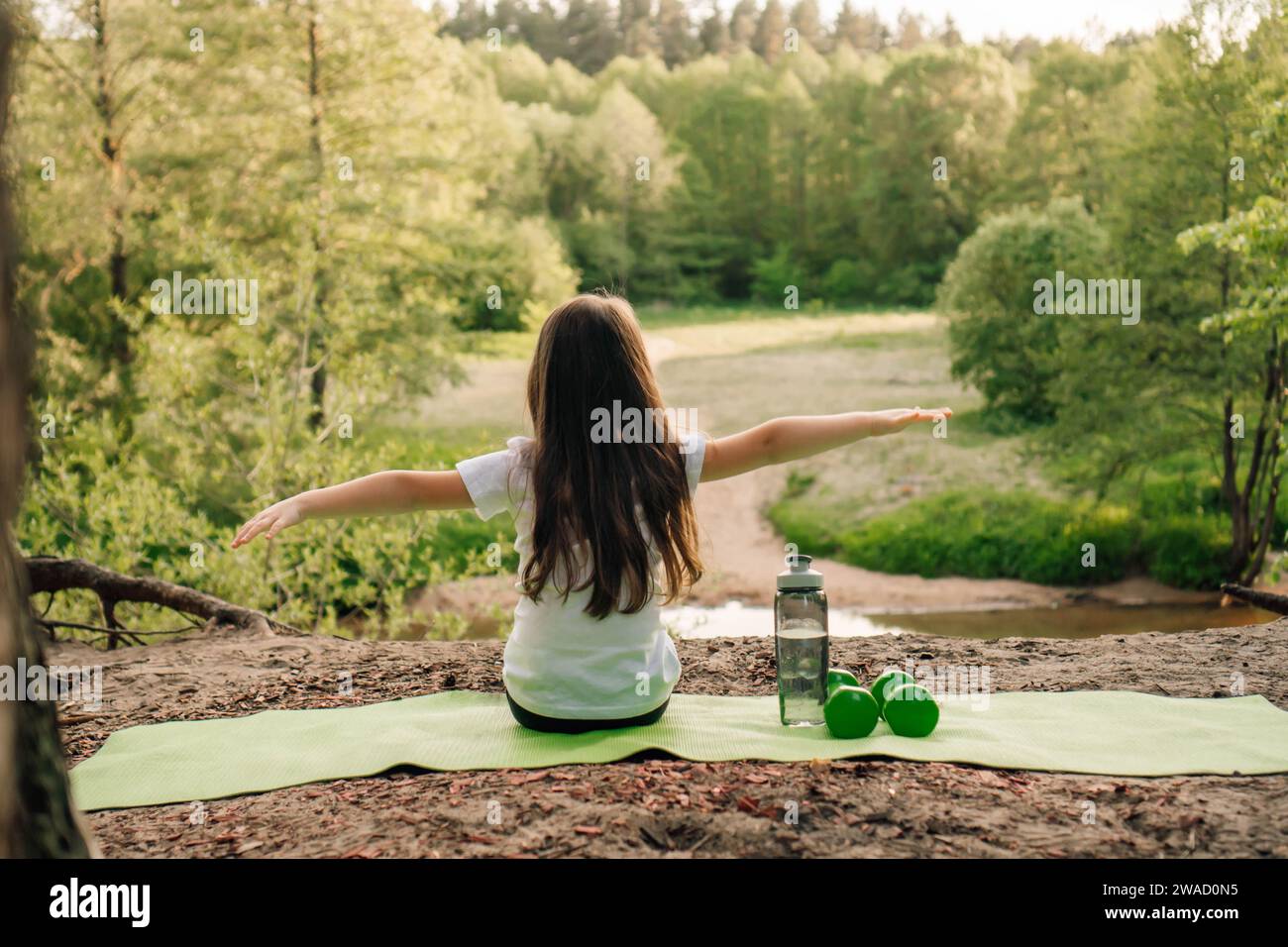 Rear view of brunette little girl with arms wide open sitting on green ...