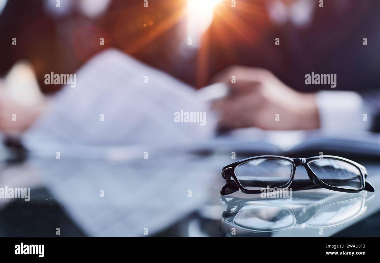 Close-up of eyeglasses on an office desk against a blurred background ...