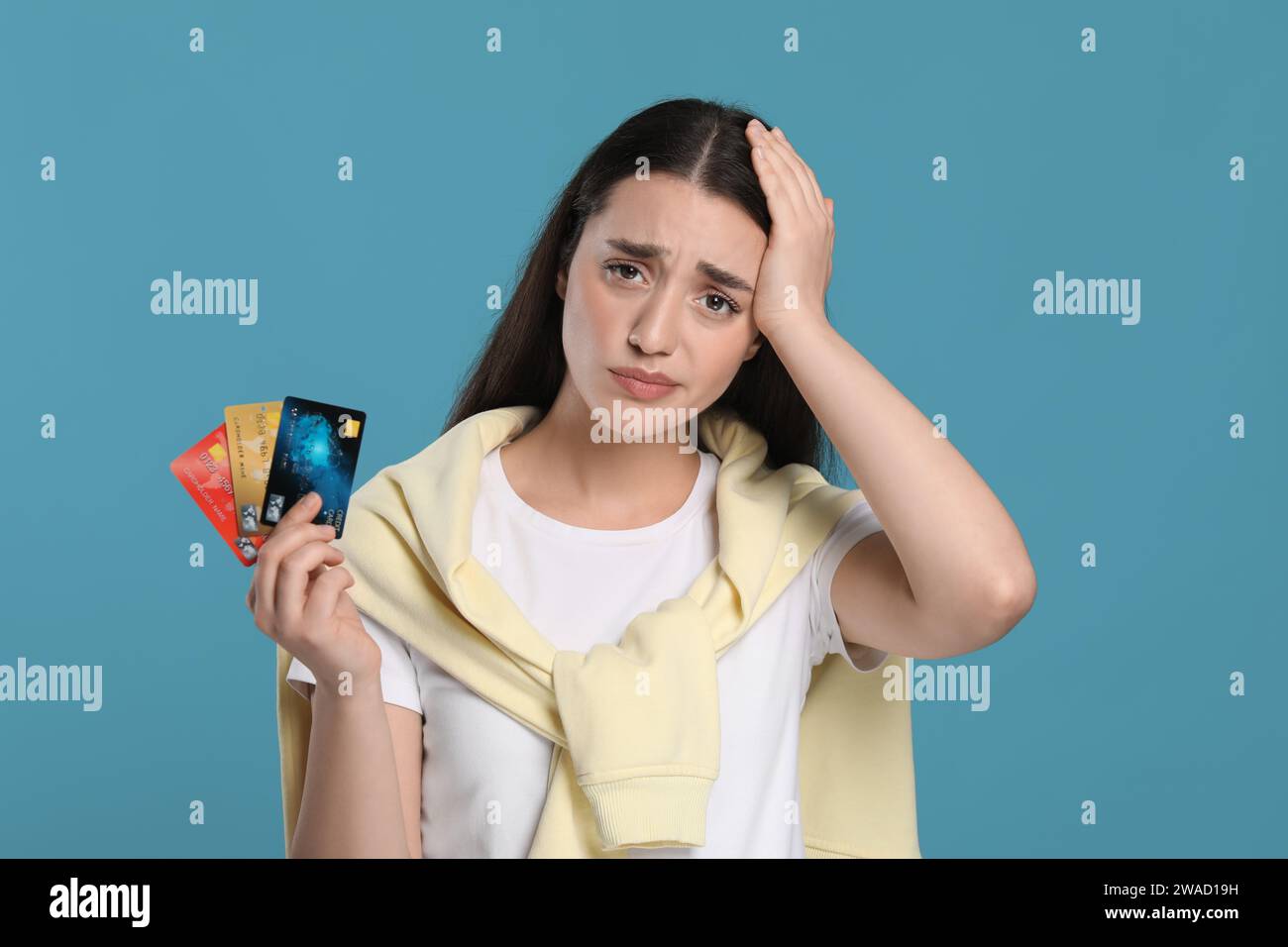 Worried woman with credit cards on light blue background. Debt problem ...