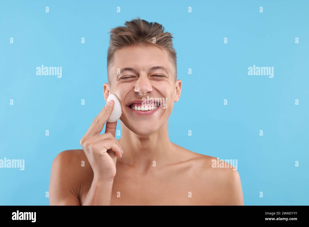 Happy young man washing his face with sponge on light blue background Stock Photo - Alamy