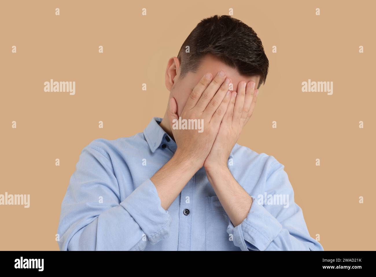 Resentful man covering face with hands on beige background Stock Photo ...