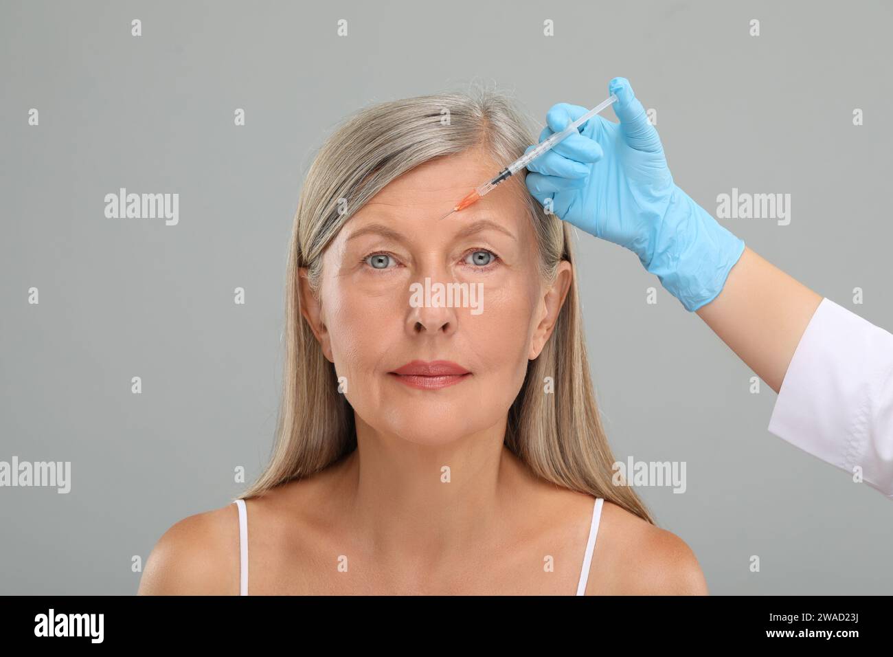 Doctor giving facial injection to senior woman on light grey background ...