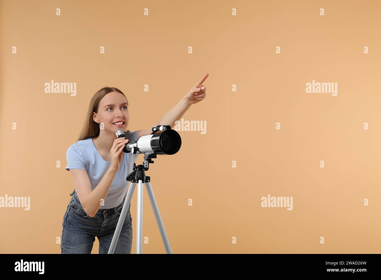 Young astronomer with telescope pointing at something on beige ...