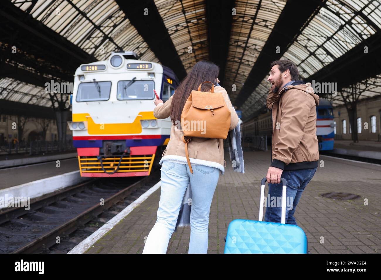 Being late. Couple with suitcase running towards train at station, back ...