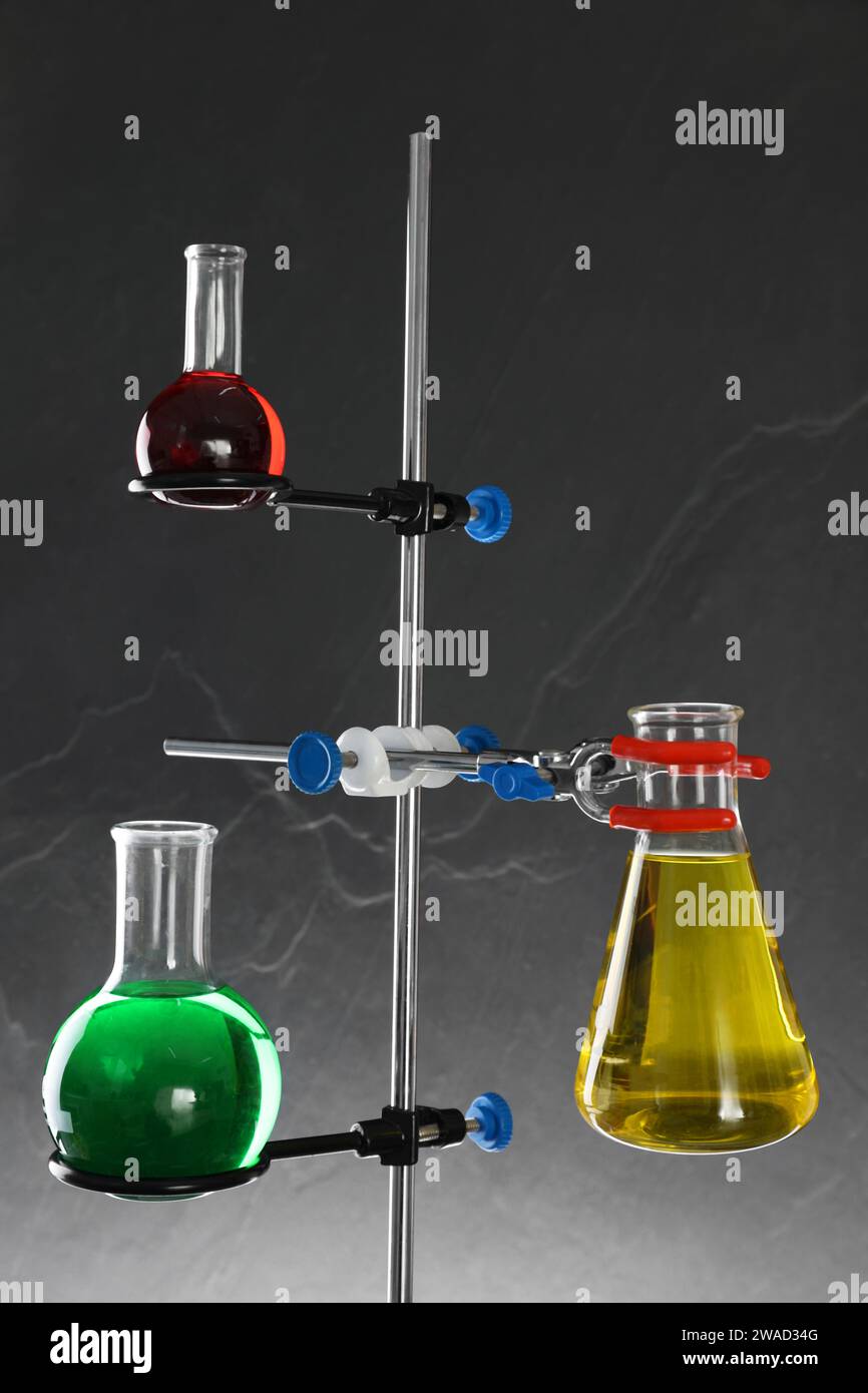 Retort stand and laboratory flasks with liquids on grey background ...