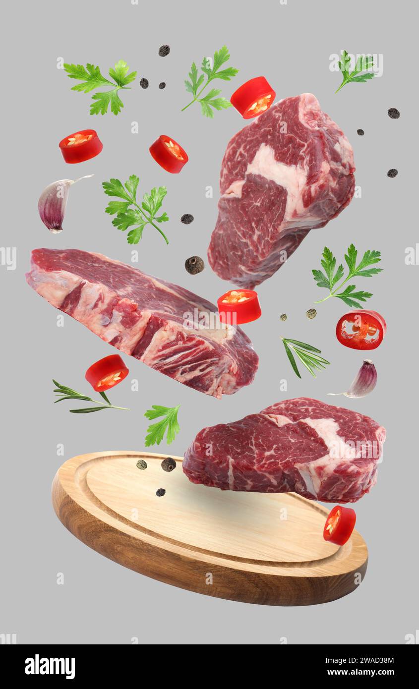Beef meat, different spices and board falling on grey background Stock ...
