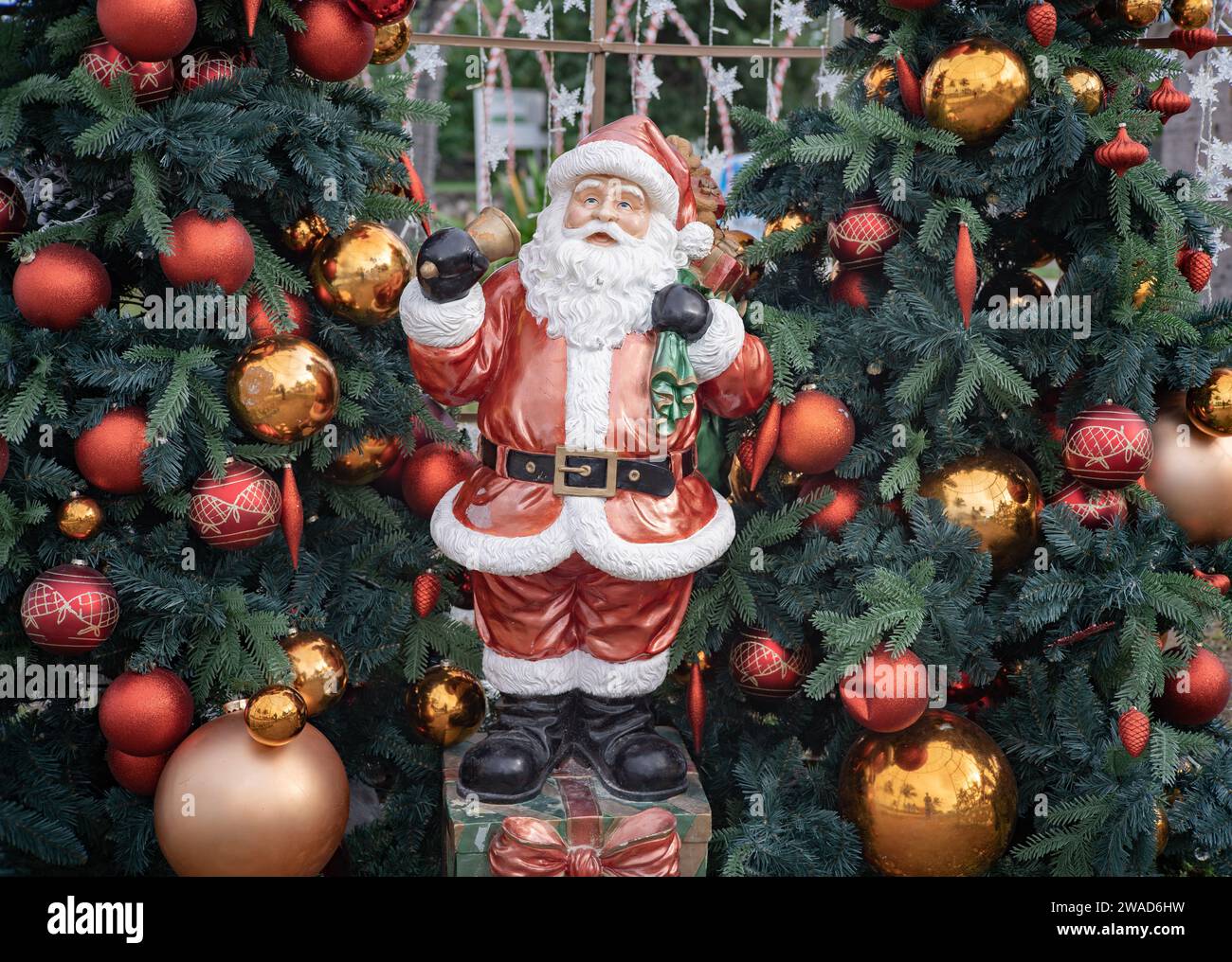 Santa Clause statue next to two Christmas trees Stock Photo - Alamy