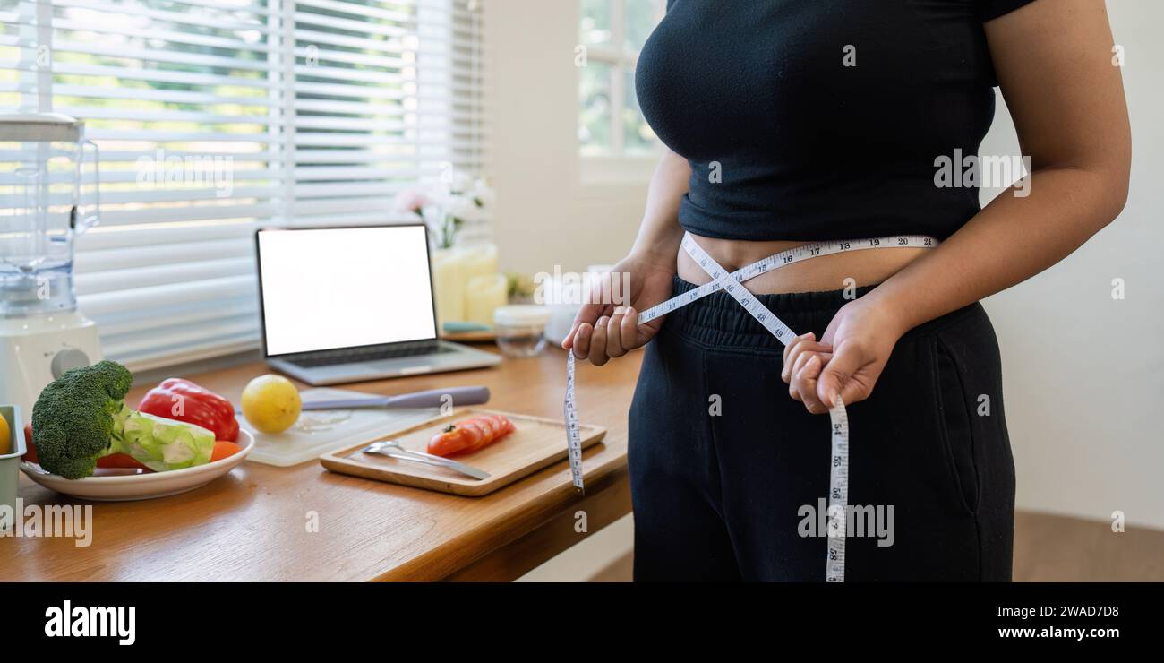 overweight Asian woman measuring her hip while learning to make salad ...